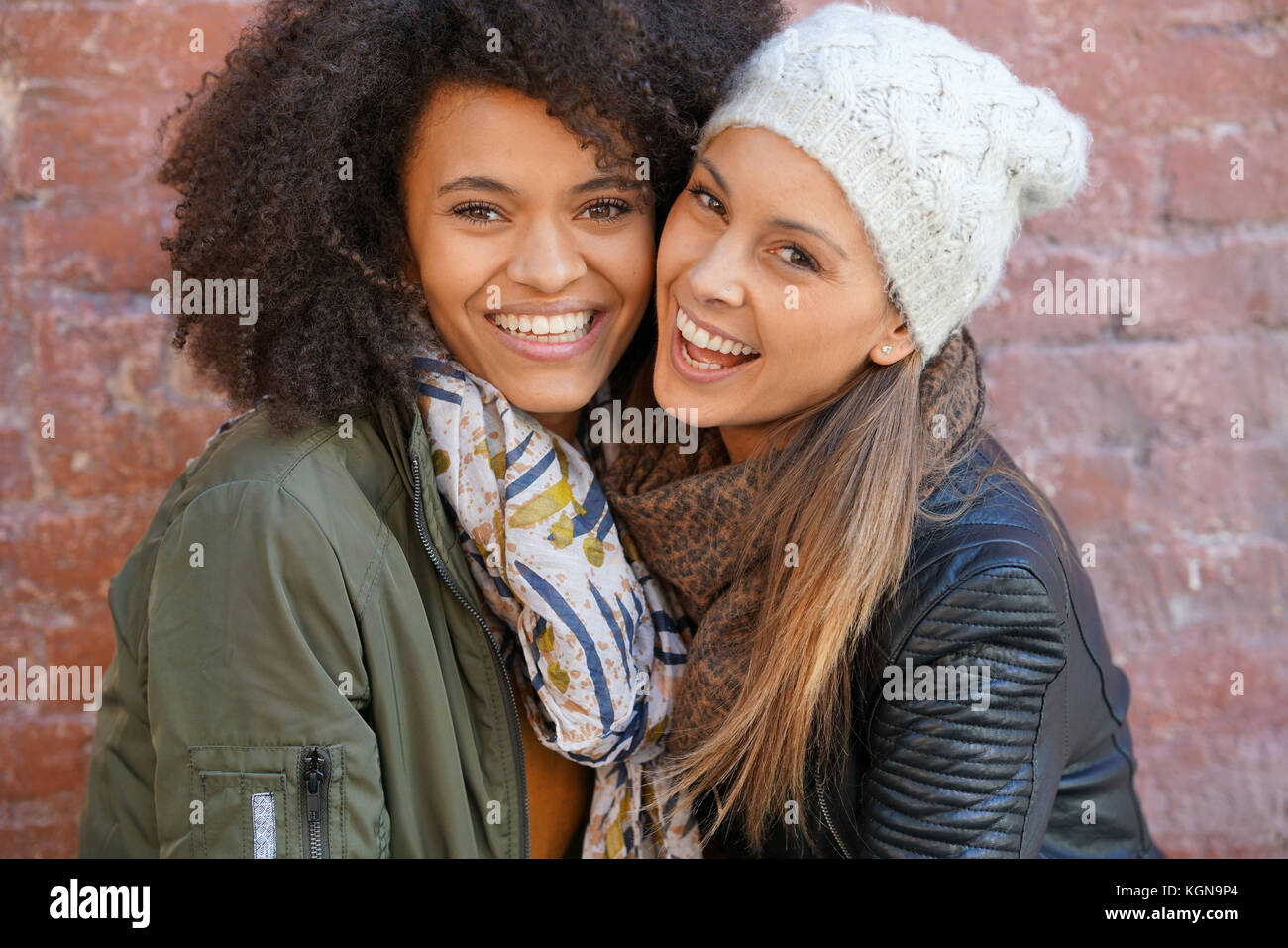 Portrait of trendy girls hugging in front of brick wall Stock Photo - Alamy
