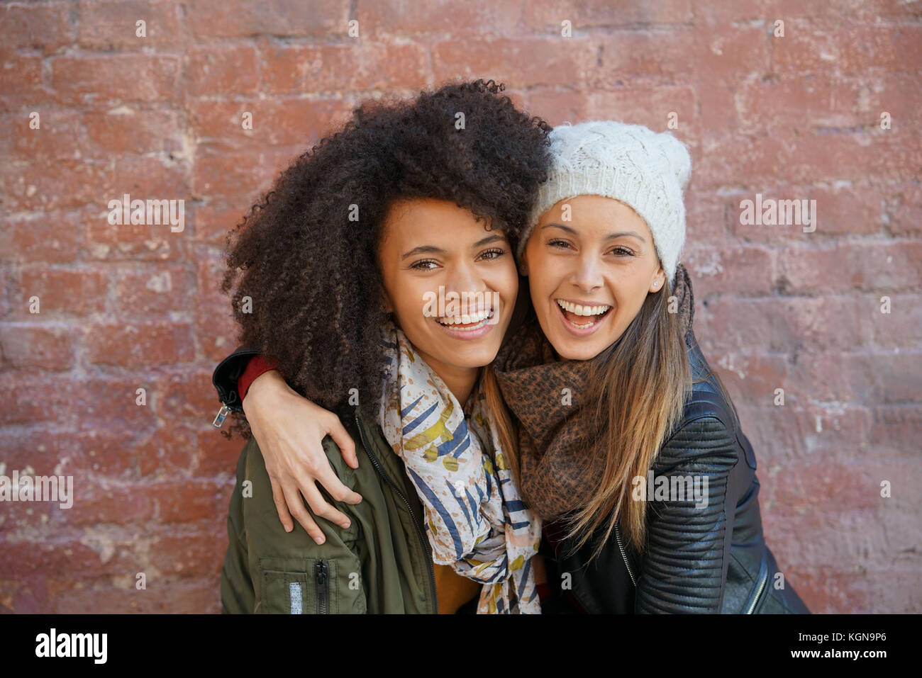 Portrait of trendy girls hugging in front of brick wall Stock Photo - Alamy