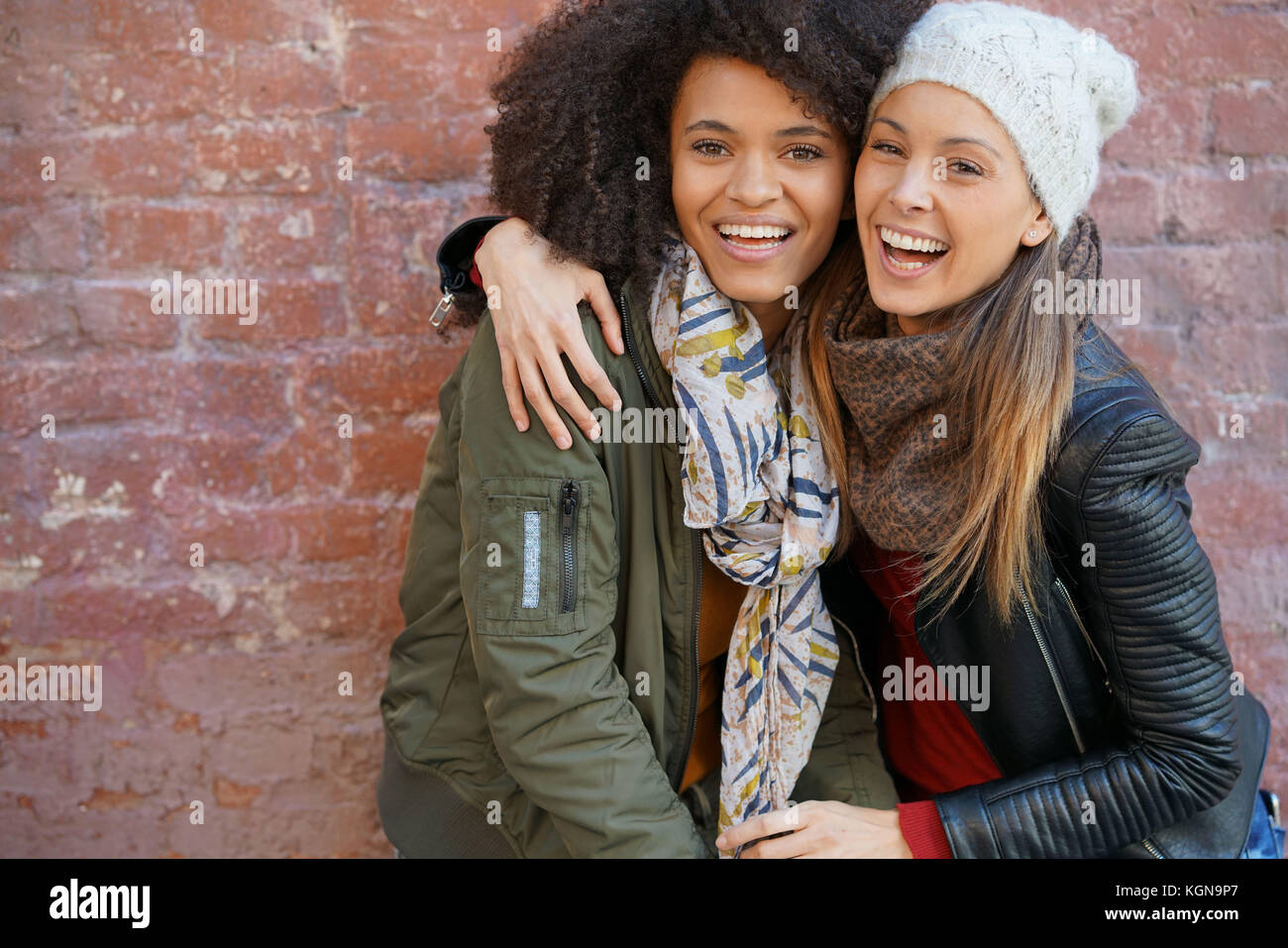 Portrait of trendy girls hugging in front of brick wall Stock Photo - Alamy