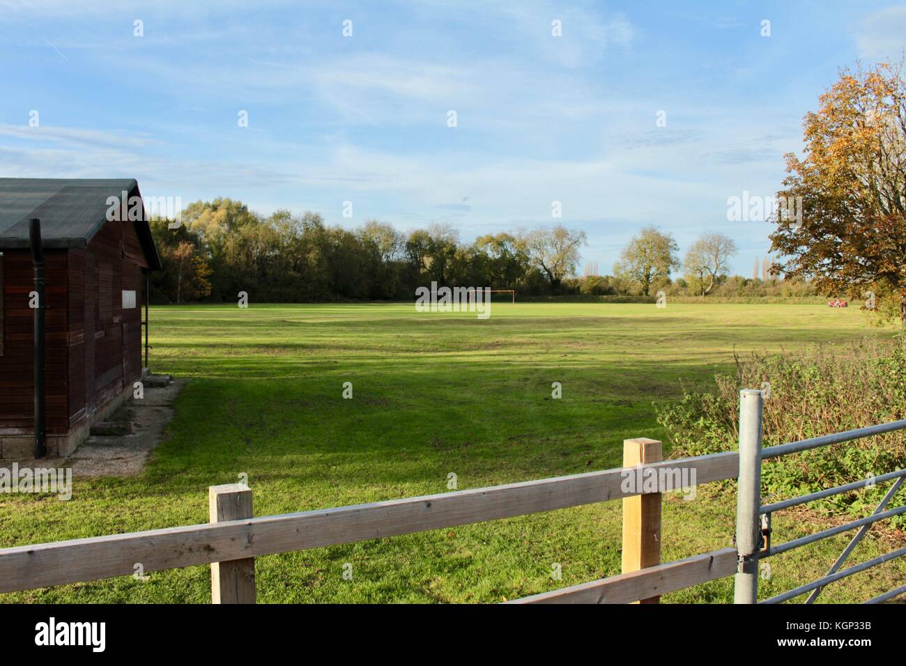 Large, empty, newly mown English village playing field through fence ...