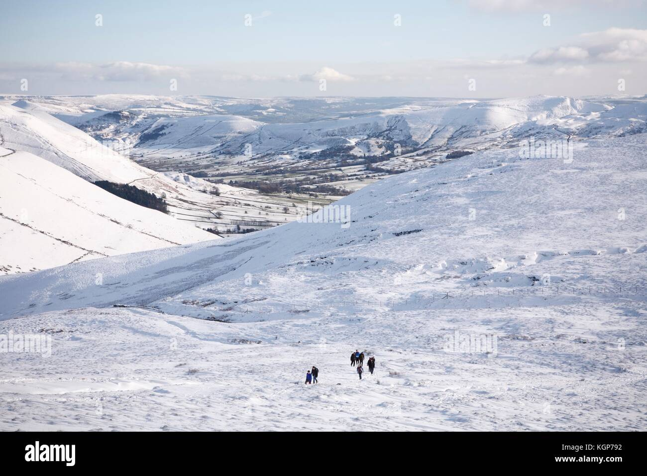 A group of people hiking on Kinder Scout in winter with Edale valley in ...