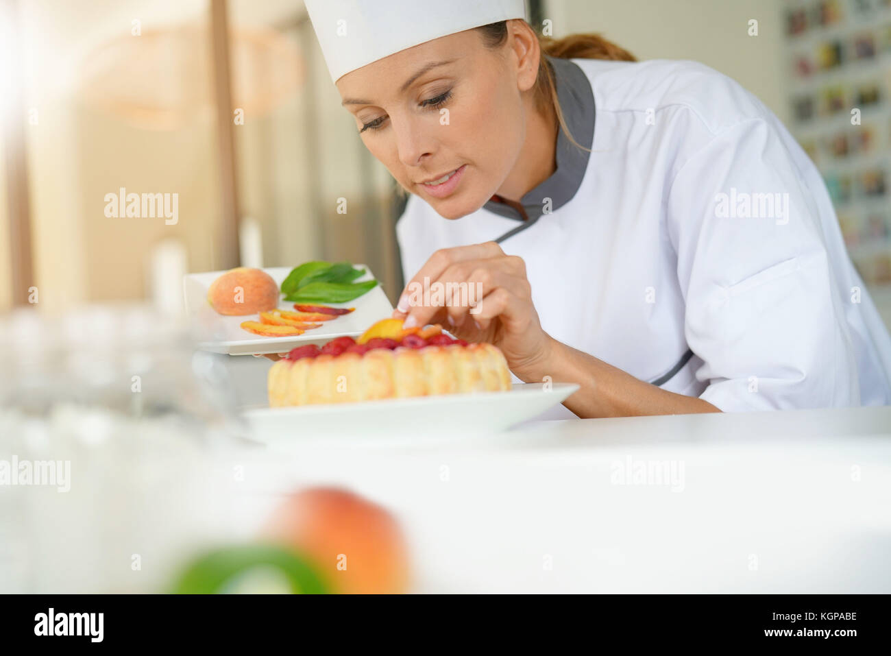 Pastry chef in professional kitchen decorating raspberry cake with ...