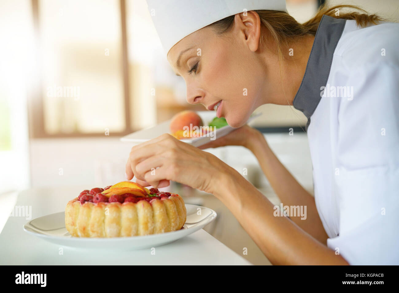 Pastry chef in professional kitchen decorating raspberry cake with ...