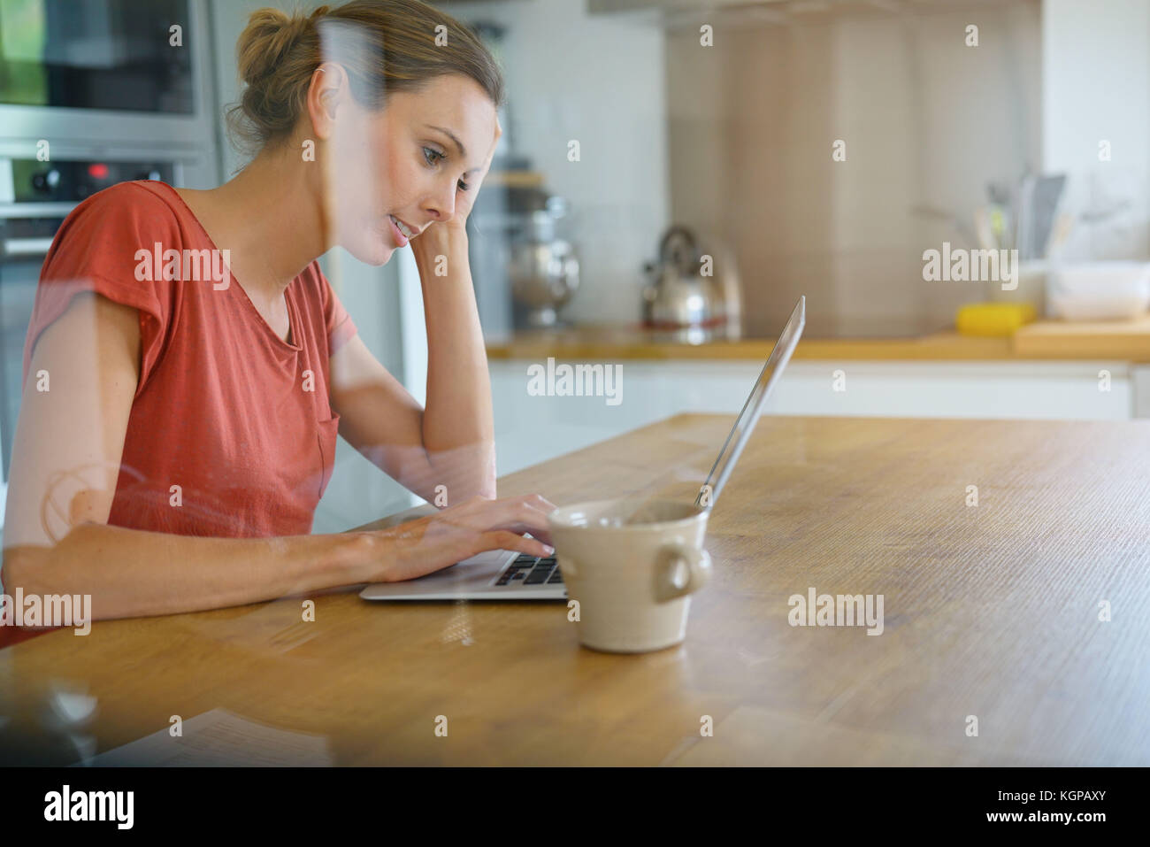 Woman sitting in kitchen connected with laptop Stock Photo - Alamy