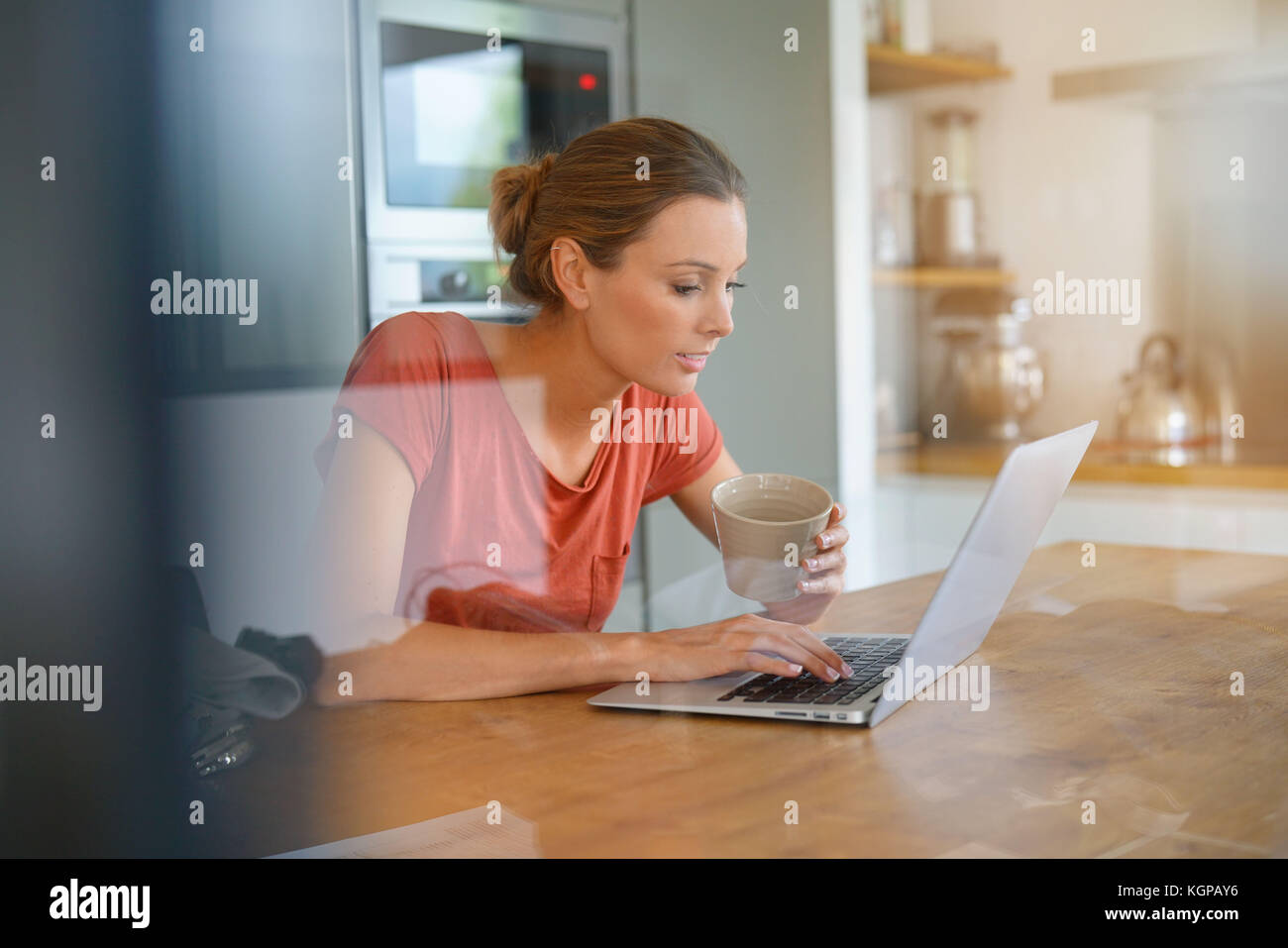 Woman sitting in kitchen connected with laptop Stock Photo - Alamy