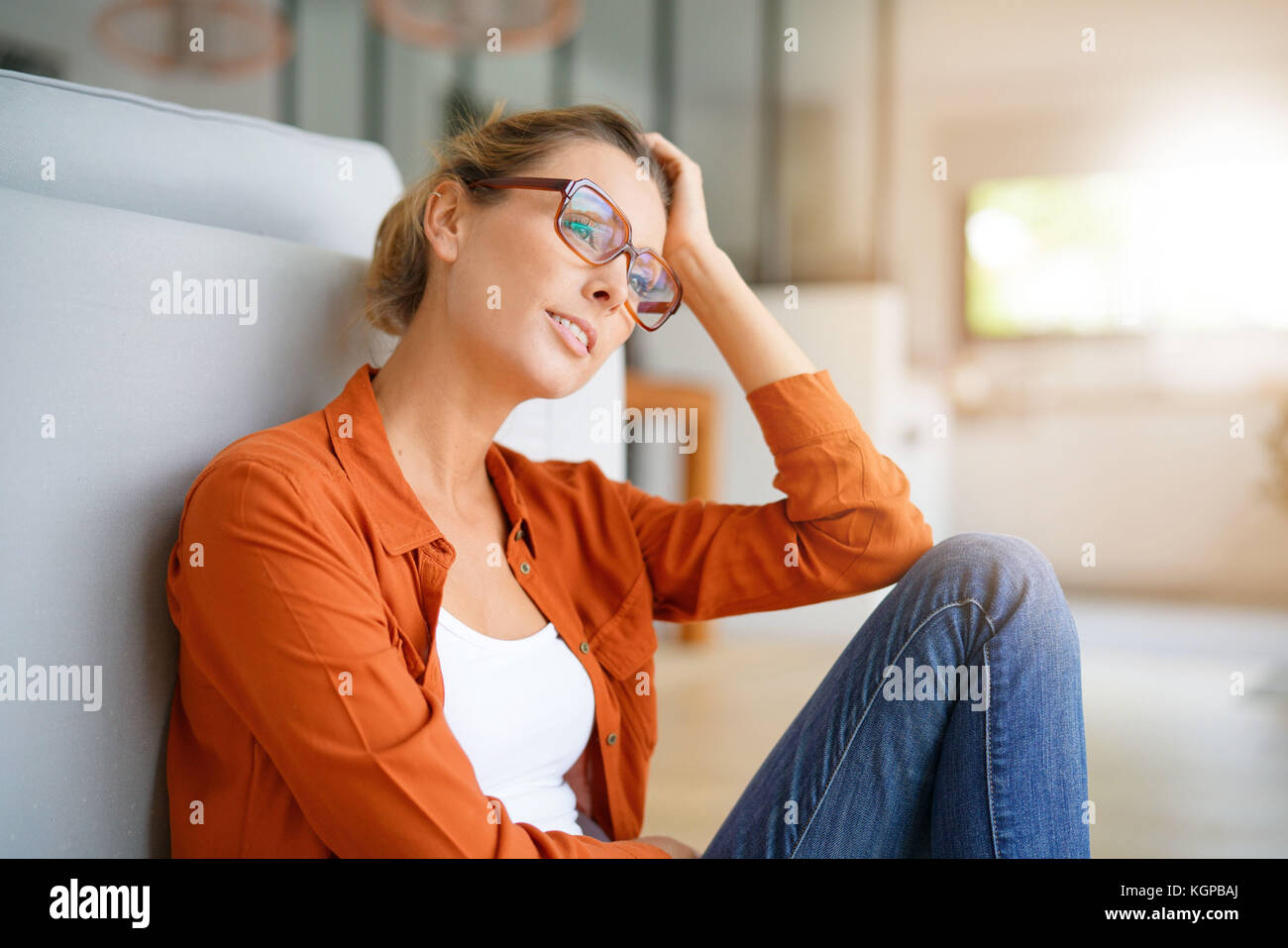 Cheerful Girl With Trendy Eyeglasses Sitting On Floor At Home Stock