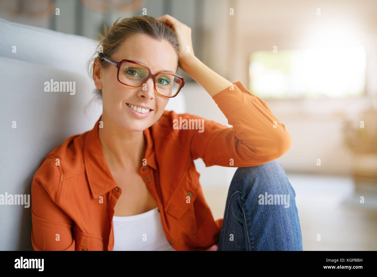 Cheerful Girl With Trendy Eyeglasses Sitting On Floor At Home Stock