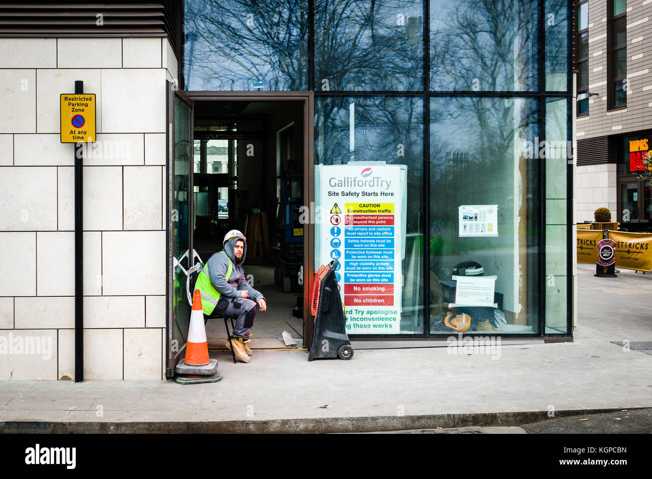 A watchman at a construction site keeps warm in front of a fire ...