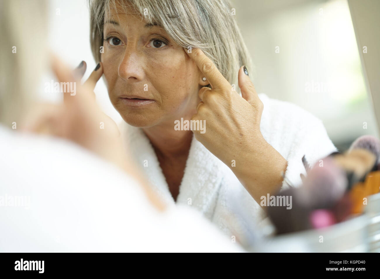 Senior woman in front of mirror looking at her skin and wrinkles Stock ...