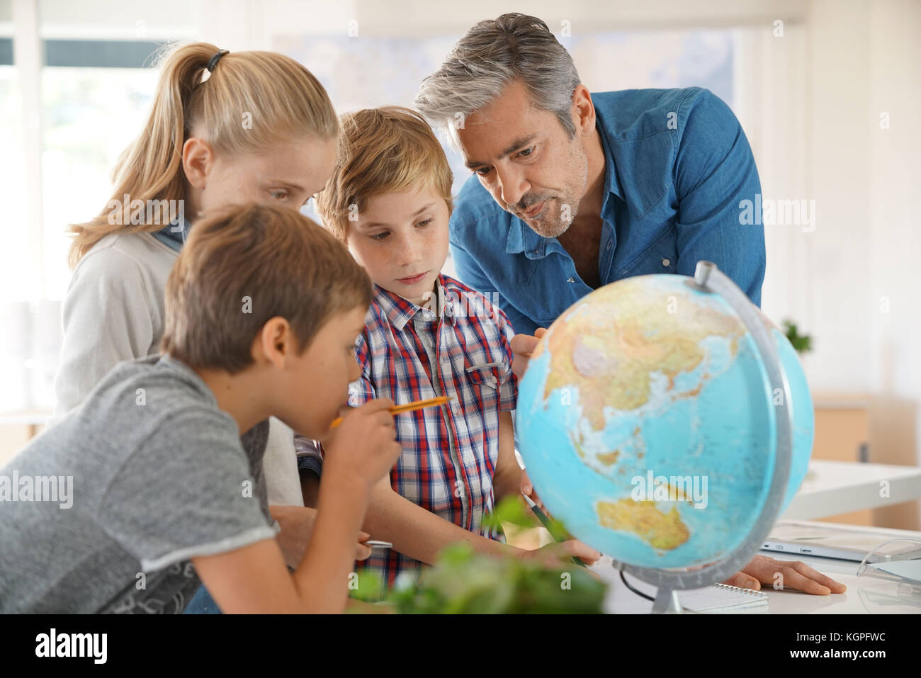 Teacher with kids in geography class looking at globe Stock Photo - Alamy