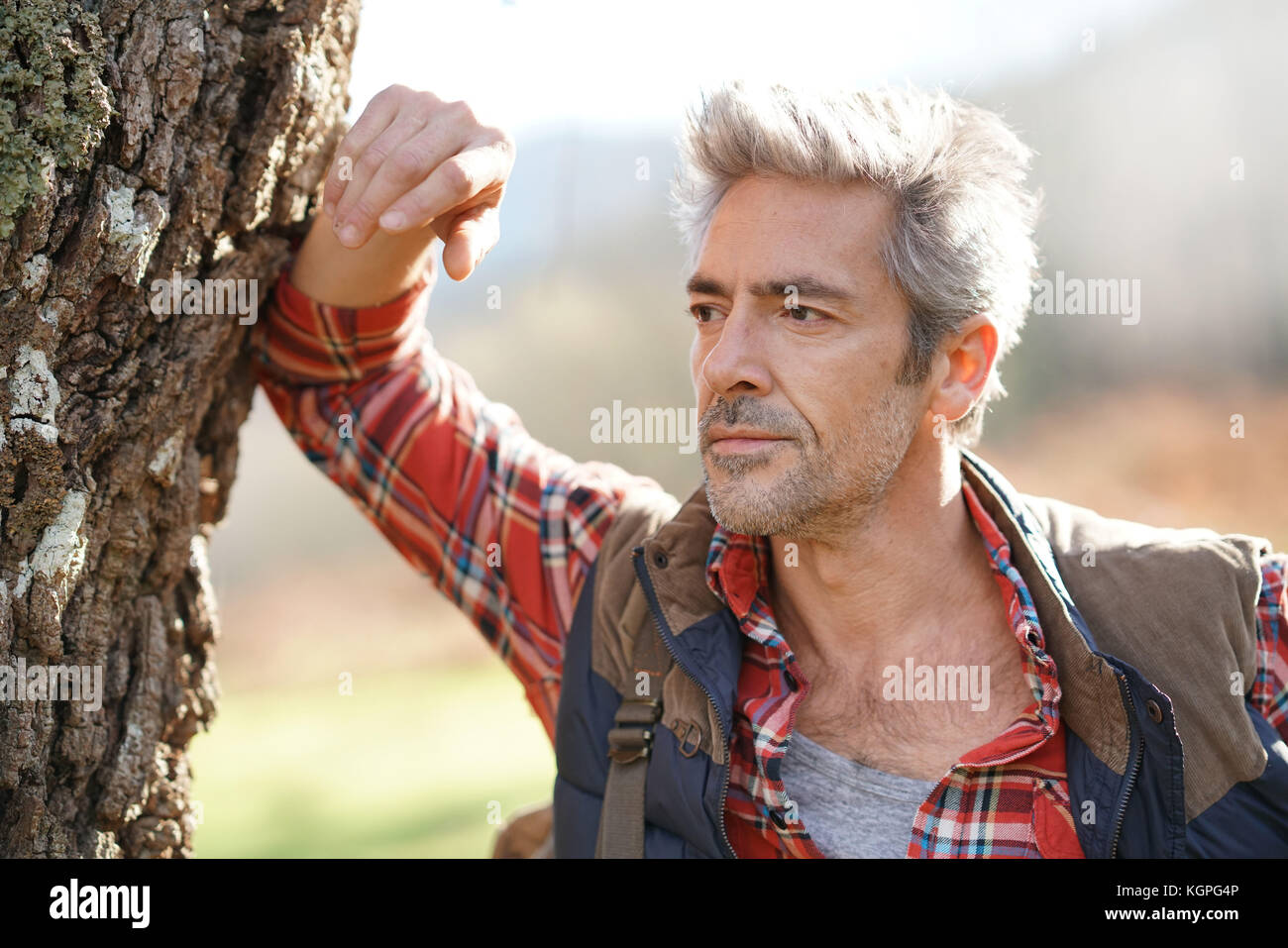 Hiker relaxing by tree on trekking journey Stock Photo - Alamy