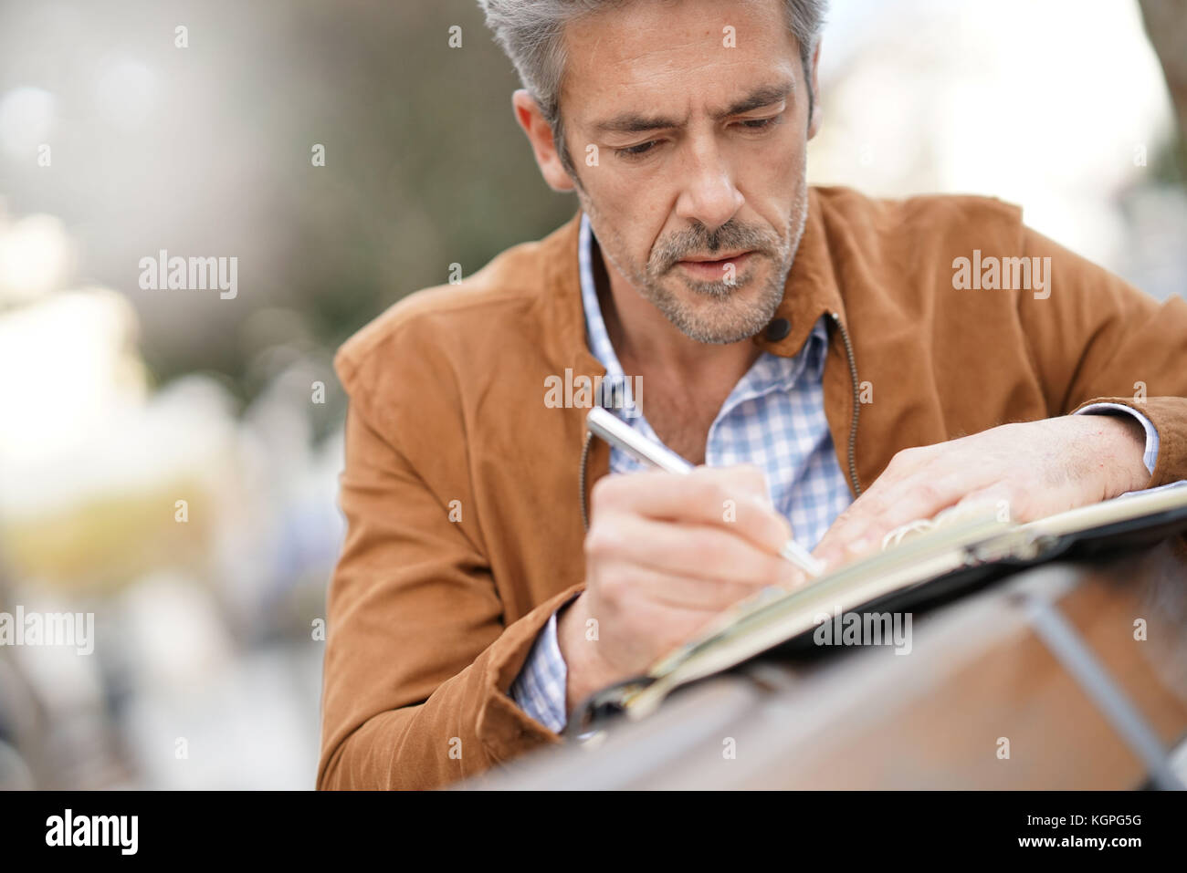 Businessman sitting on public bench, writing on agenda Stock Photo - Alamy