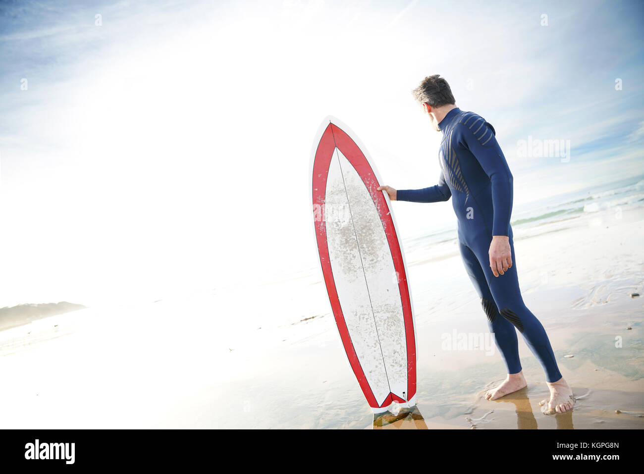 Surfer standing on sandy beach, next to surfboard Stock Photo - Alamy