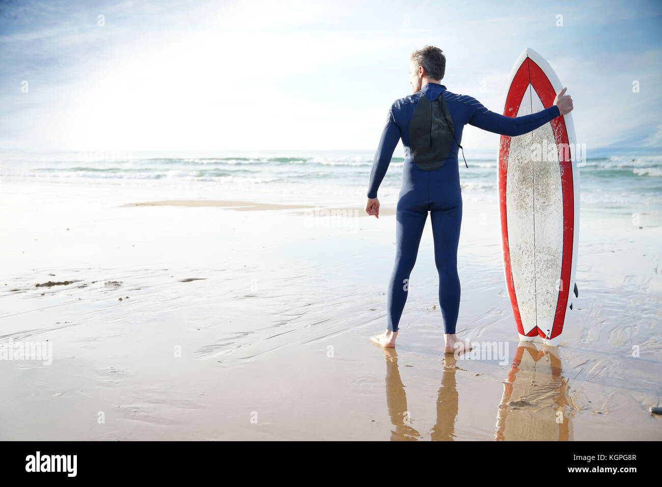 Surfer standing on sandy beach, next to surfboard Stock Photo - Alamy