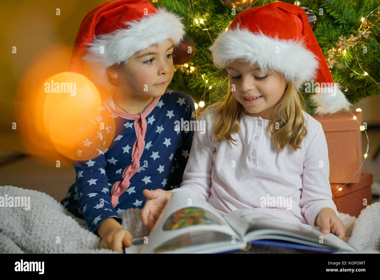 Kids reading book by Christmas tree Stock Photo - Alamy