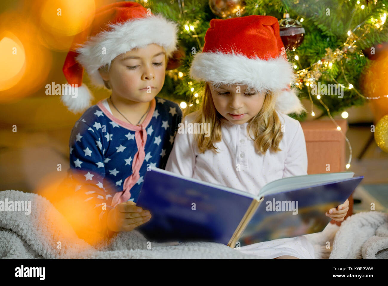 Kids reading book by Christmas tree Stock Photo - Alamy