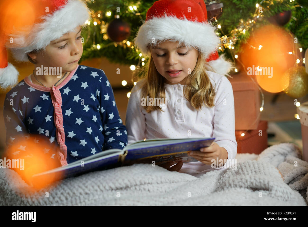 Kids reading book by Christmas tree Stock Photo - Alamy