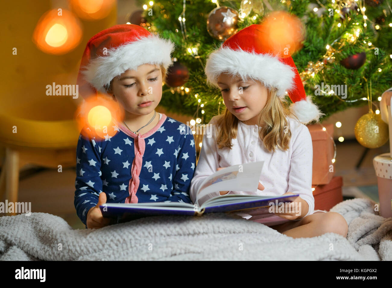 Kids reading book by Christmas tree Stock Photo - Alamy