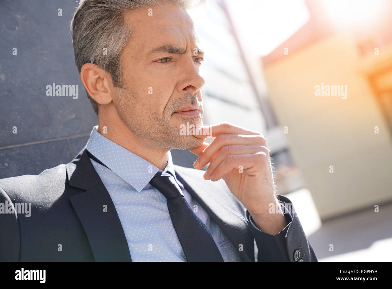 Portrait of businessman waiting outside building, leant on wall Stock ...