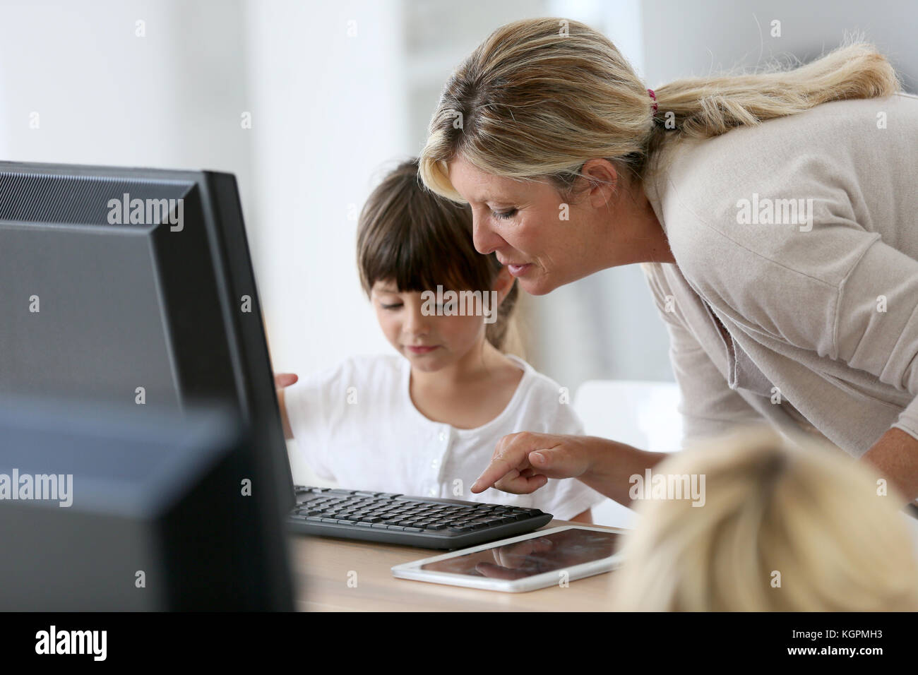 Teacher with little girl in class using computer and tablet Stock Photo ...