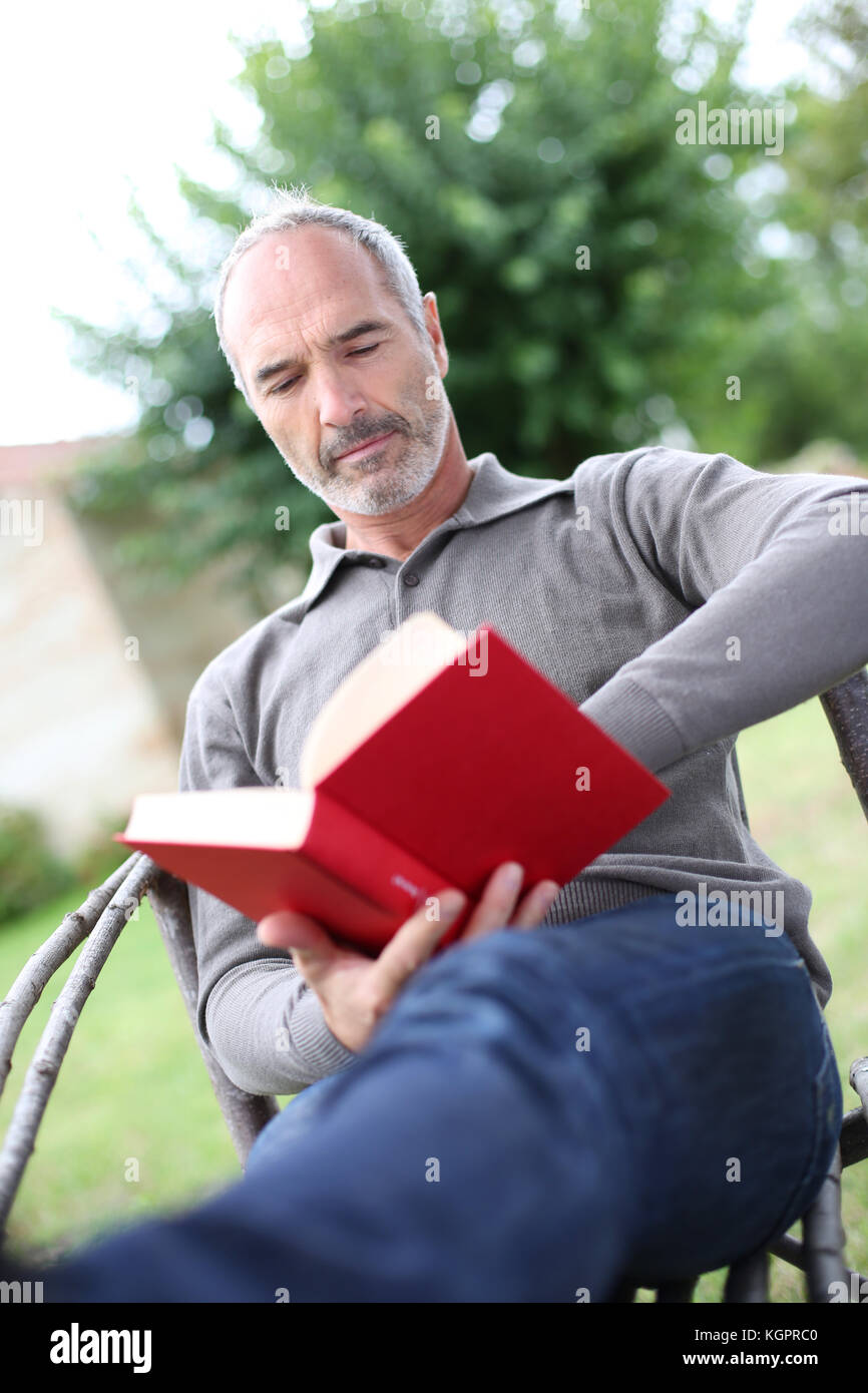 Senior man reading novel in country home garden Stock Photo - Alamy