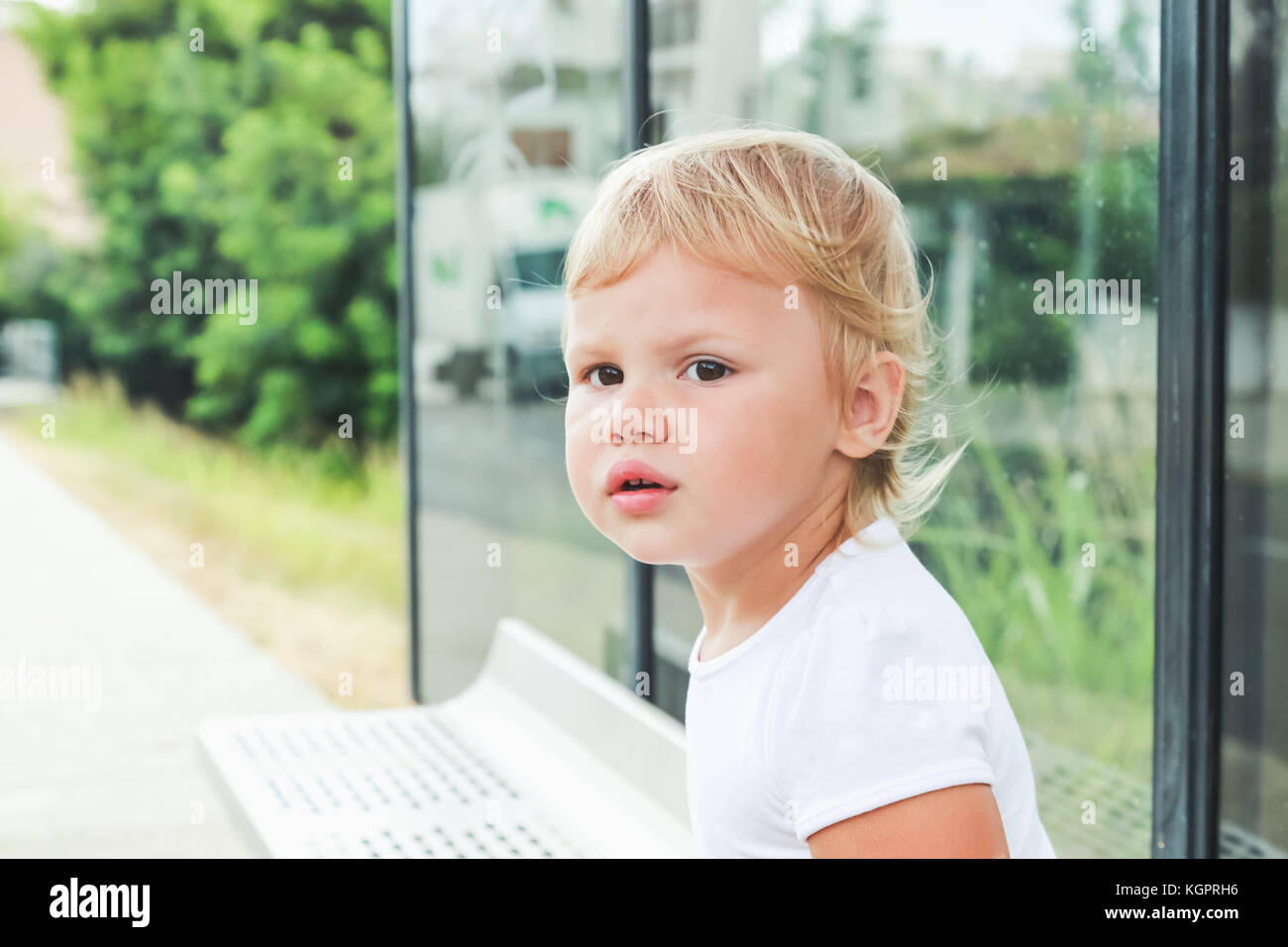 Sad Caucasian blond baby girl waits on a bus stop. Closeup portrait ...