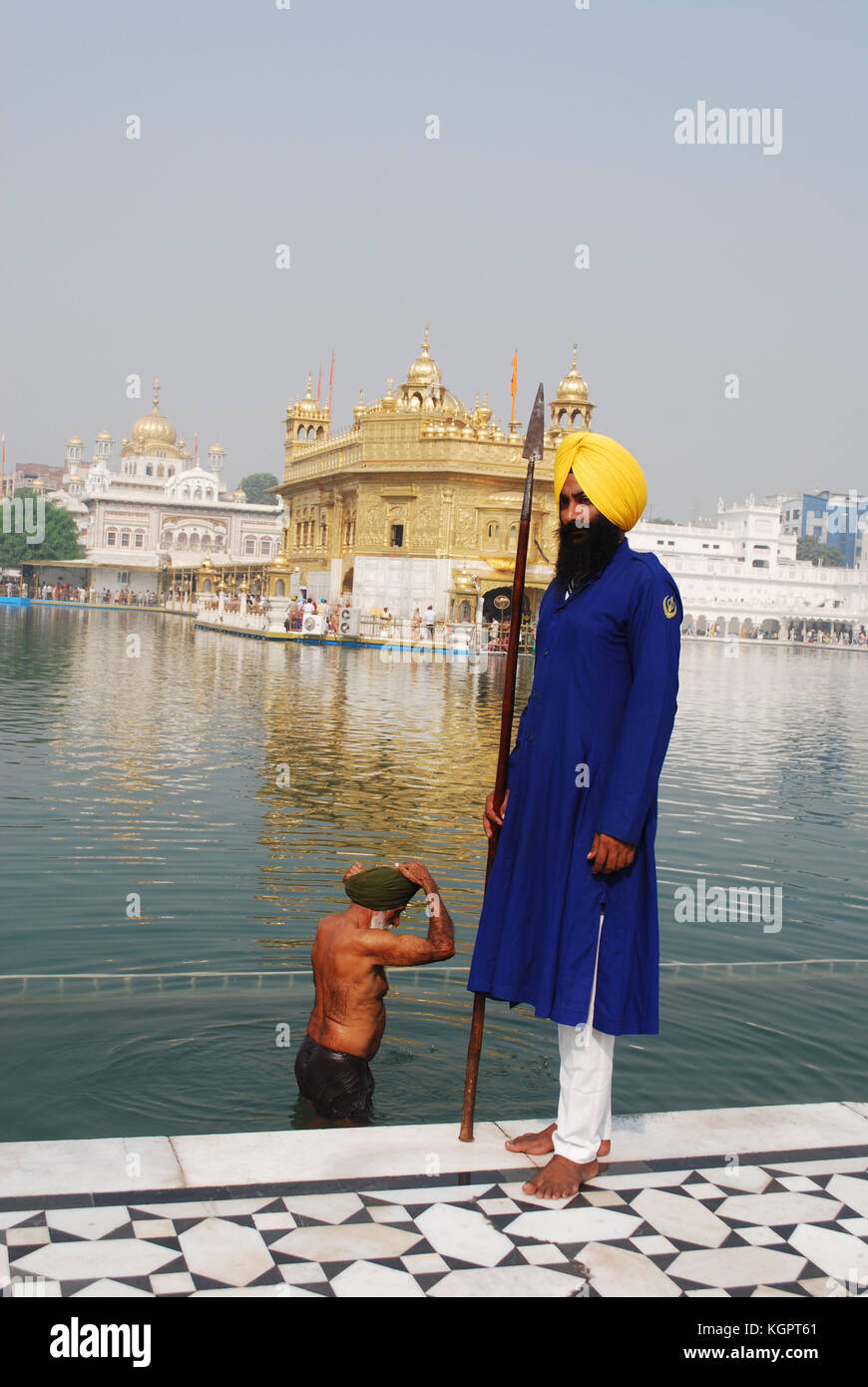 A Sikh guard with a man bathing behind in the sacred Amrit Sarovar Lake ...