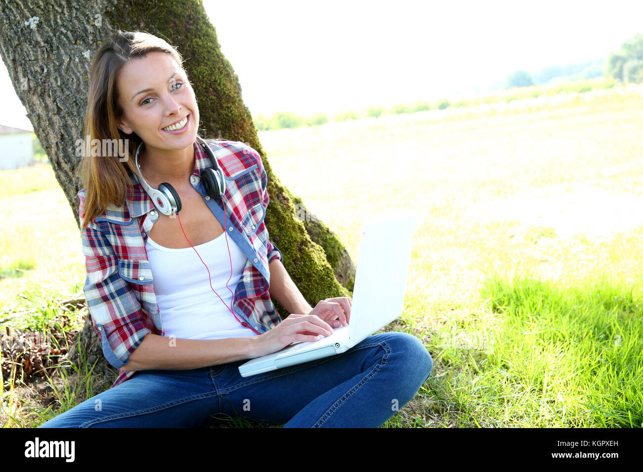 Cheerful girl sitting against tree with laptop Stock Photo - Alamy