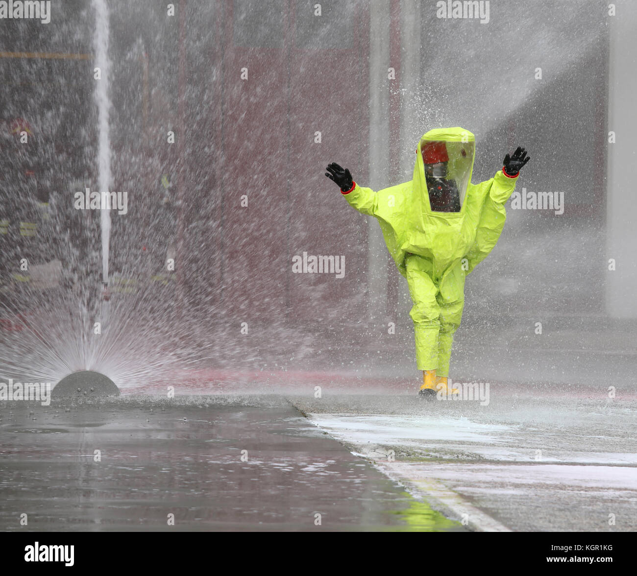 man with yellow protective suit and splashes of water to decontaminate ...
