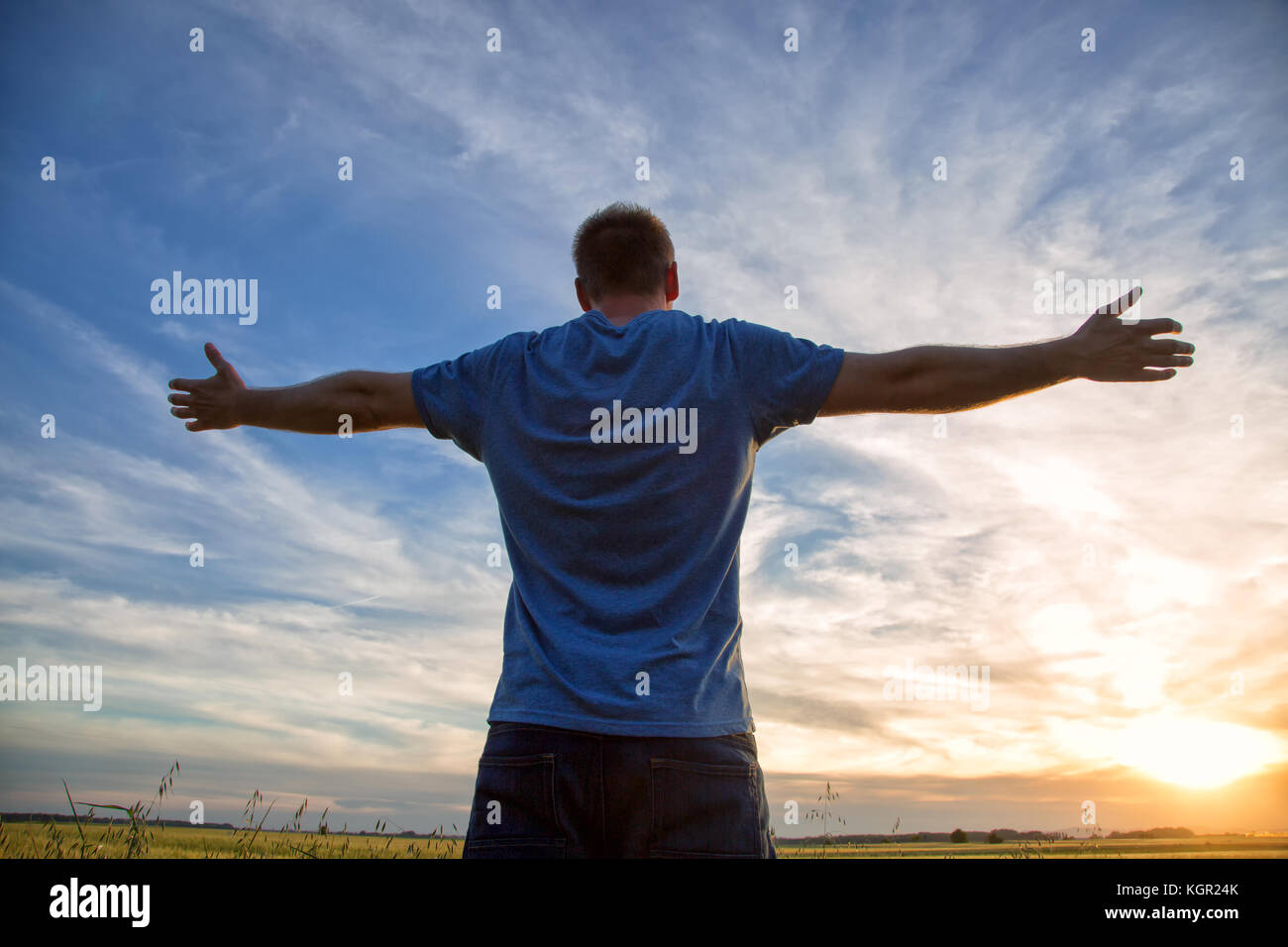 Man standing in an open field at sunset with open arms - embracing ...