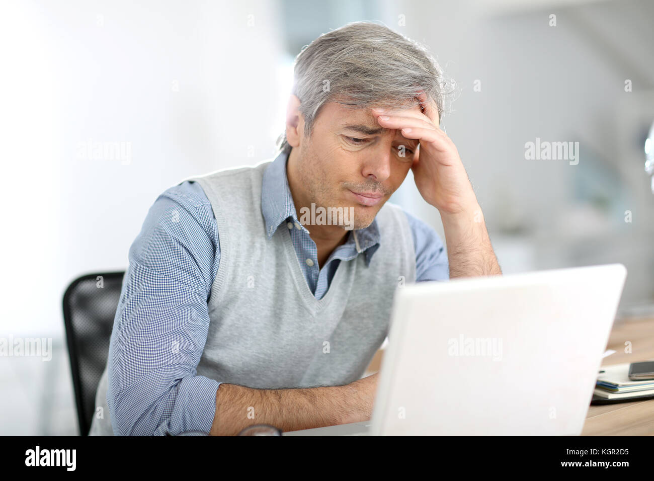 Senior businessman in front of laptop having a headache Stock Photo - Alamy