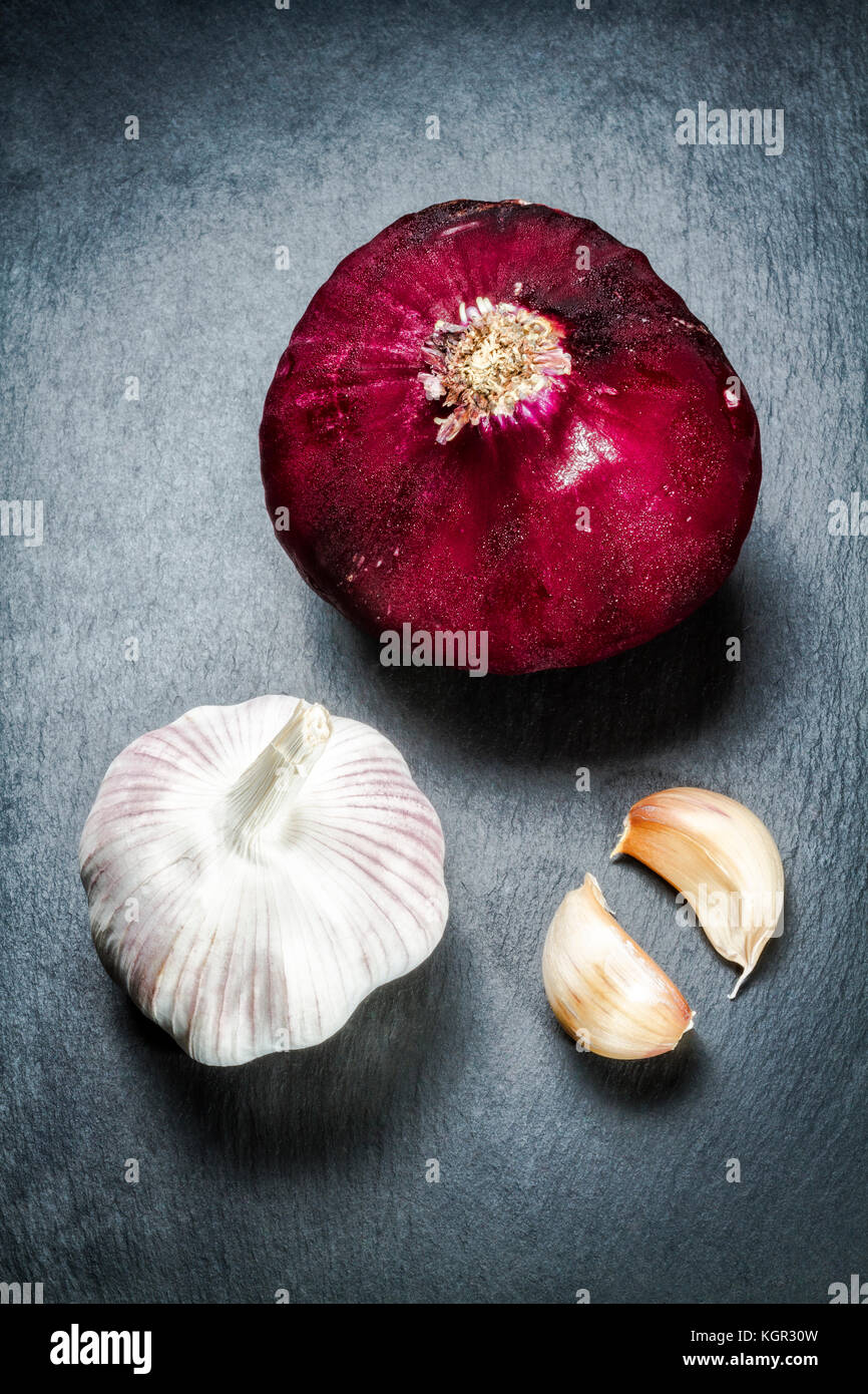 Garlic (Allium sativum) and red onion (Allium cepa) on a black slate ...