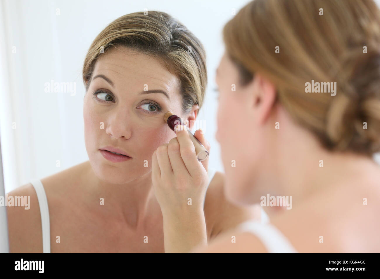Beautiful blond woman applying concealer around eyes Stock Photo - Alamy