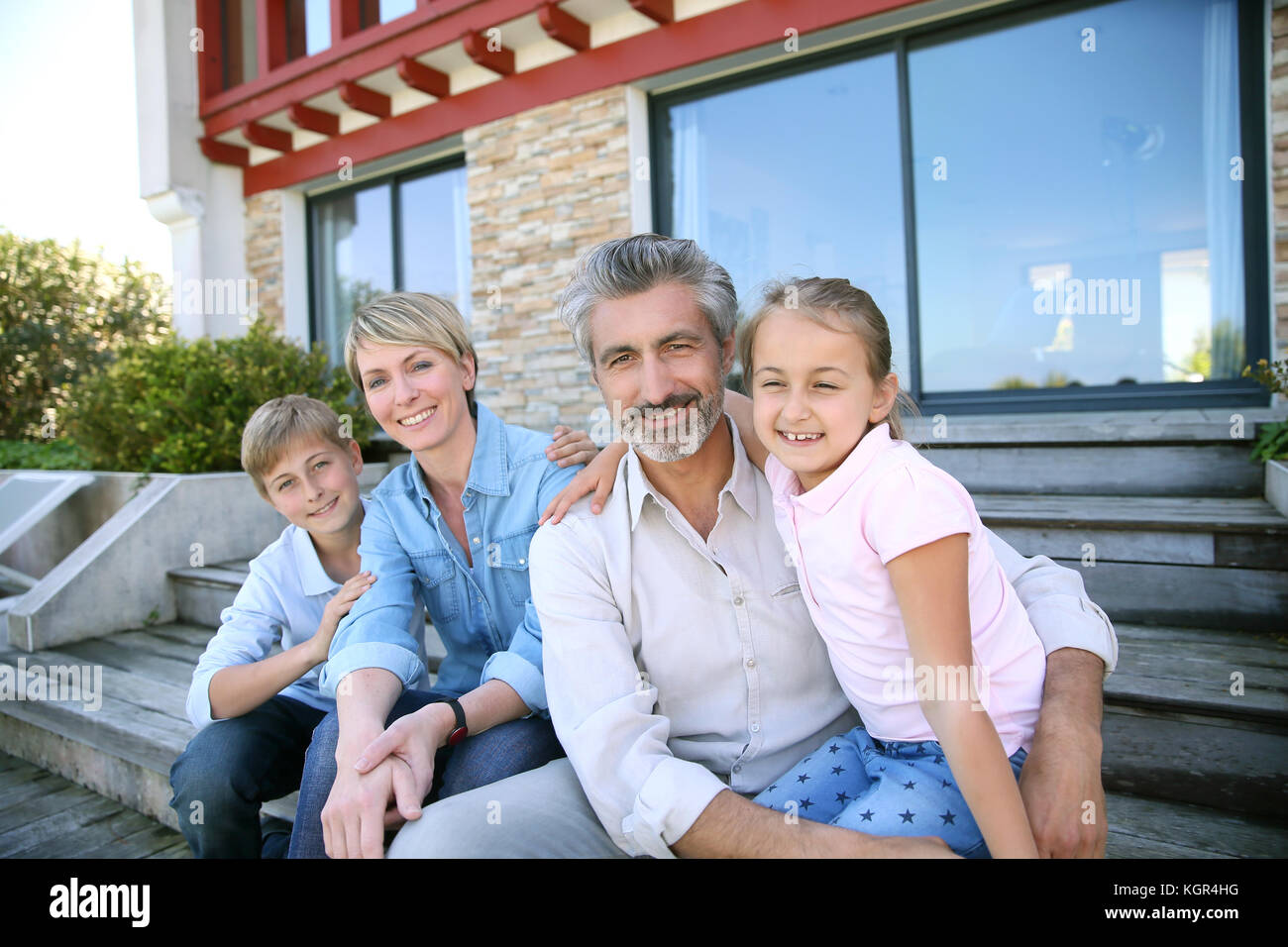 Happy family of four sitting in front of contemporary house Stock Photo ...