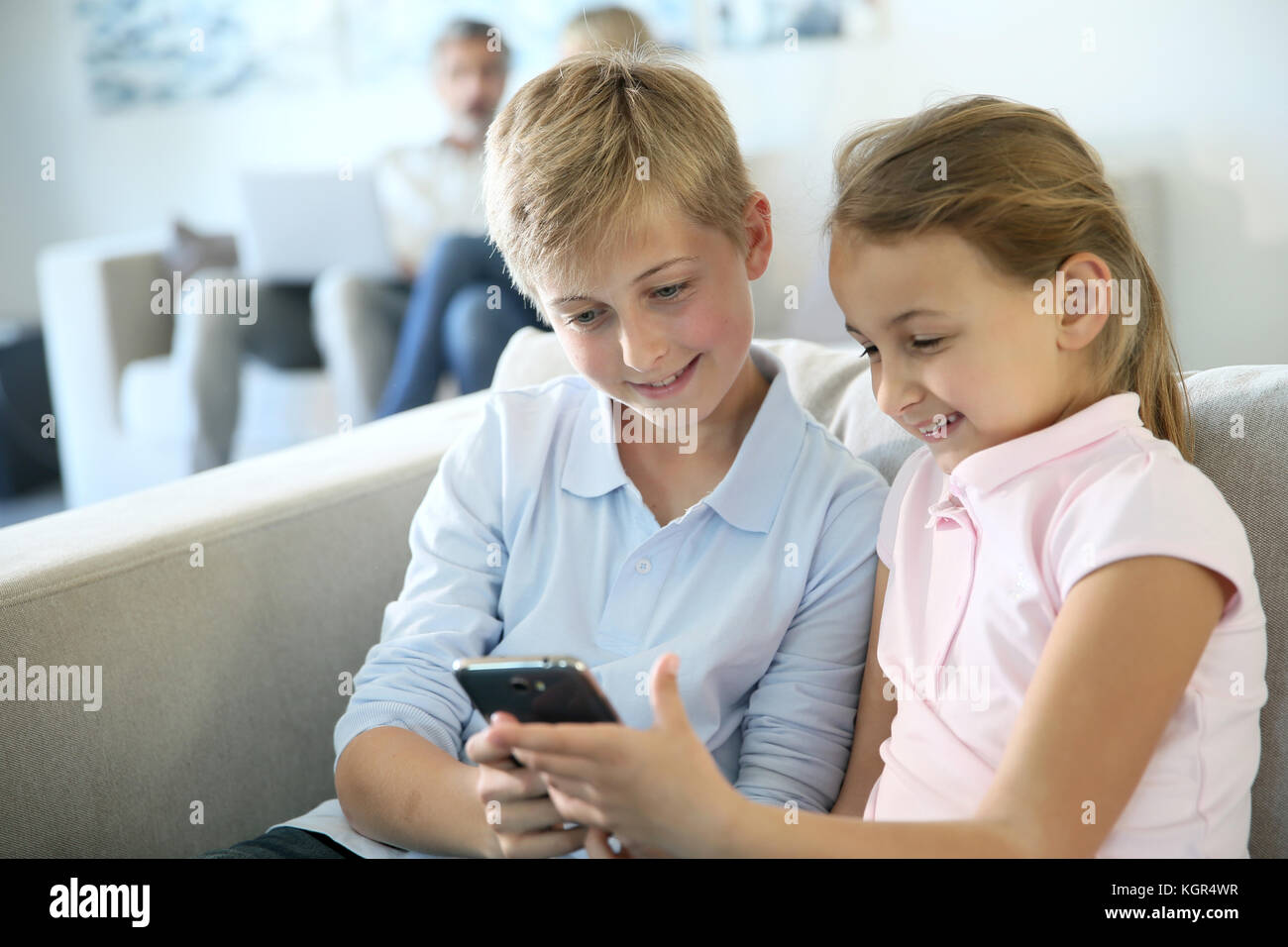 Kids playing with smartphone, parents in background Stock Photo - Alamy