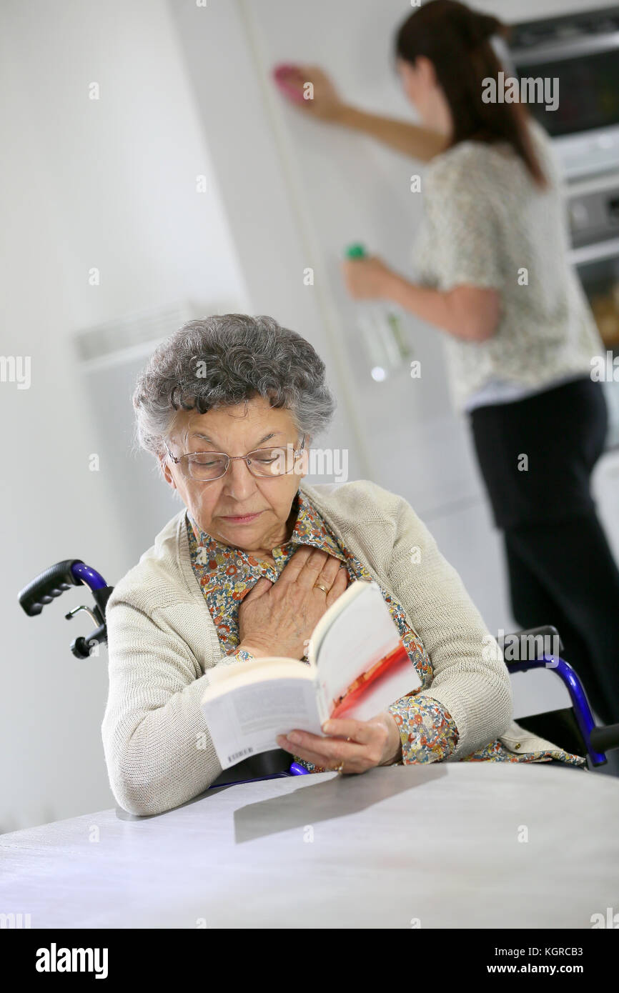 Elderly woman reading book, home helper in background Stock Photo - Alamy