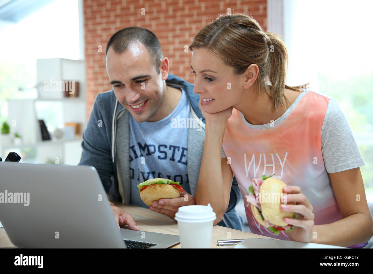 Roommates eating sandwich in front of laptop Stock Photo - Alamy