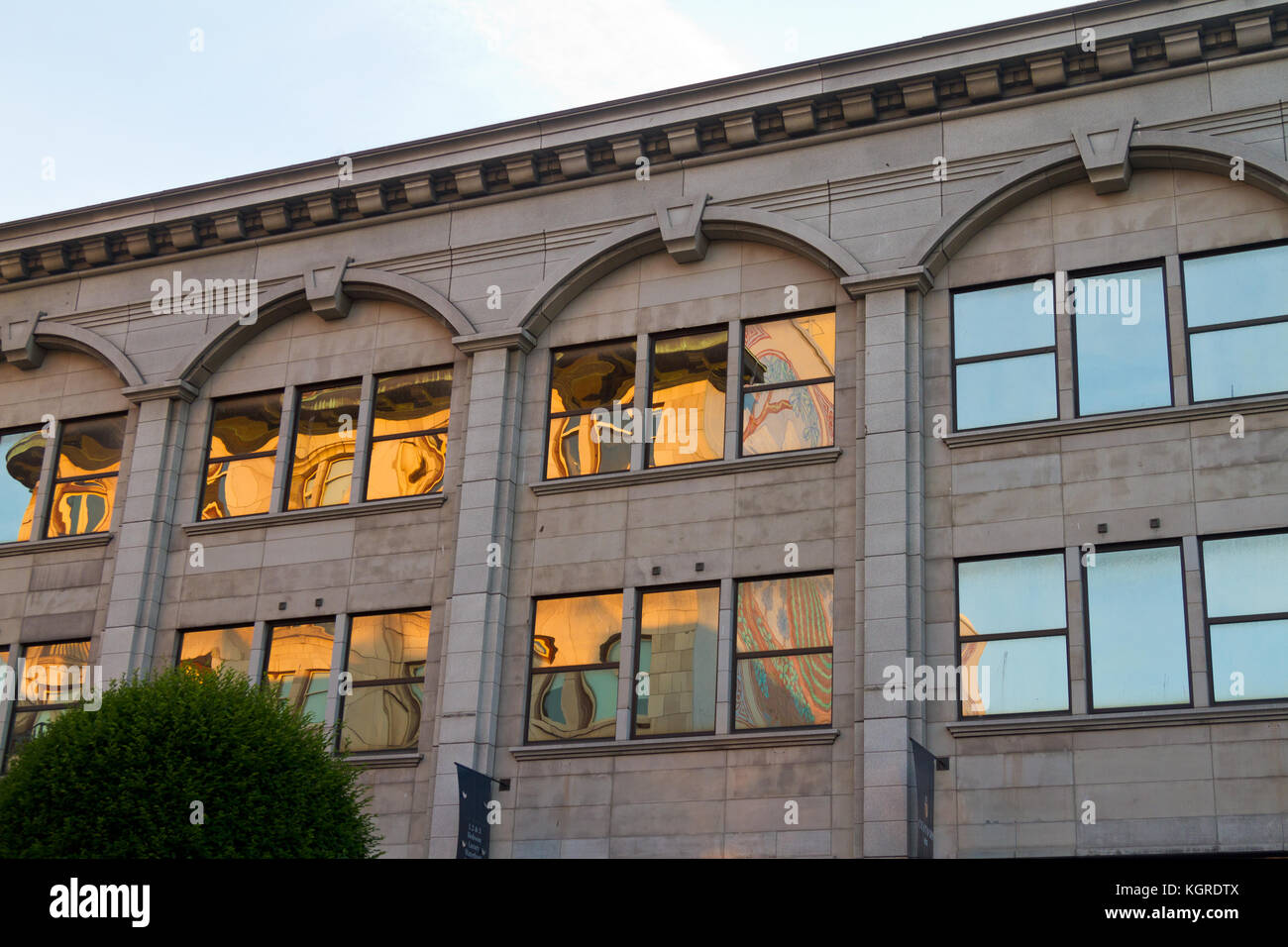 Building bathed in late afternoon light is reflected with distortion in ...
