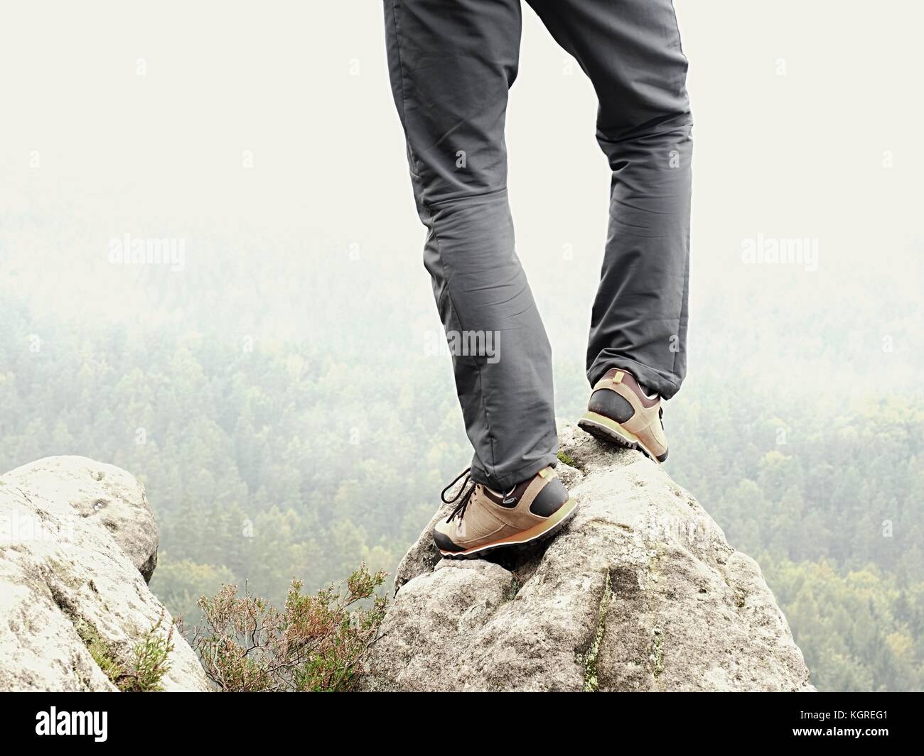 Male legs in dark hiking trousers and leather trekking shoes on peak of ...