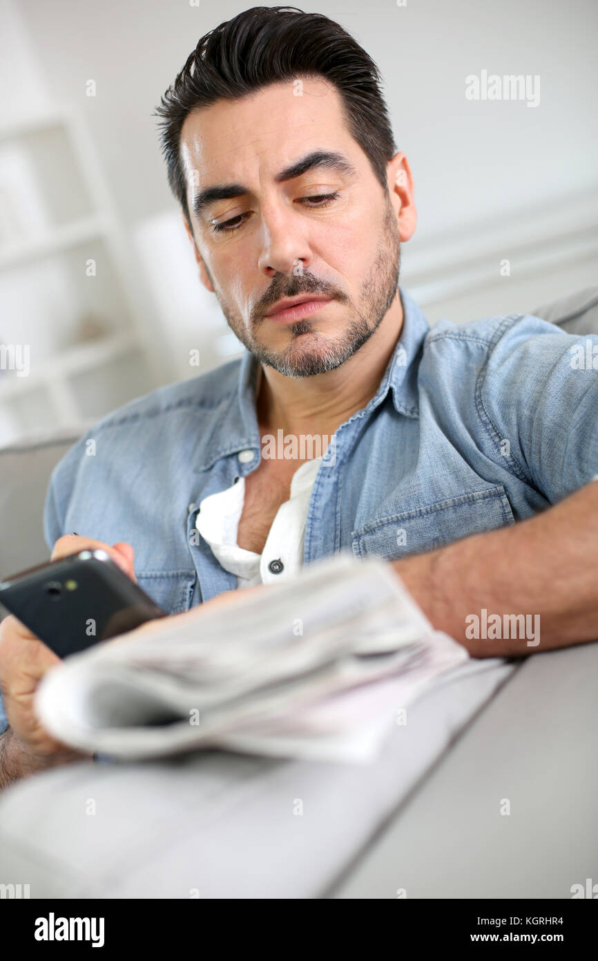 Man reading newspaper while using smartphone Stock Photo - Alamy