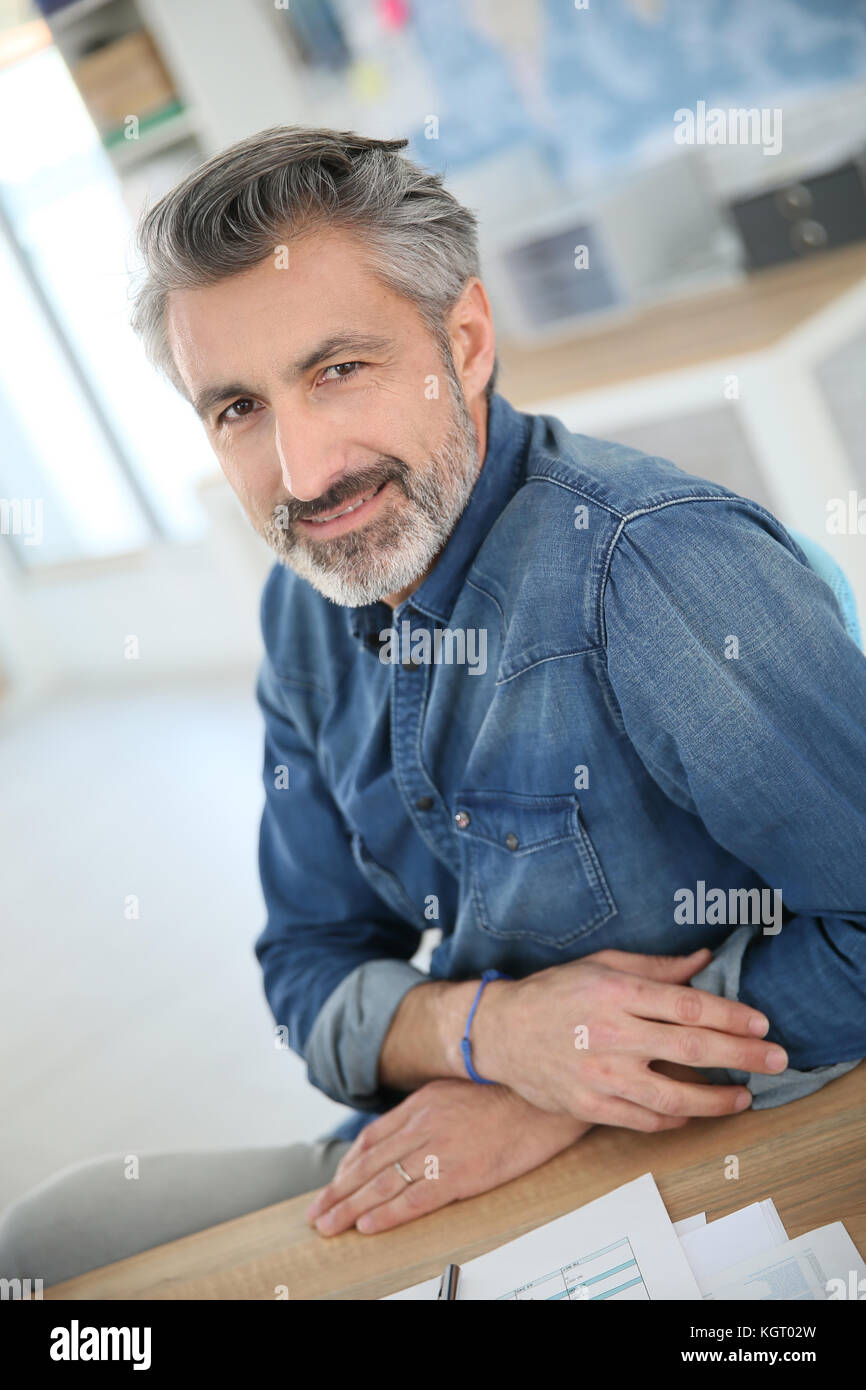 Smiling teacher sitting at desk in university office Stock Photo - Alamy