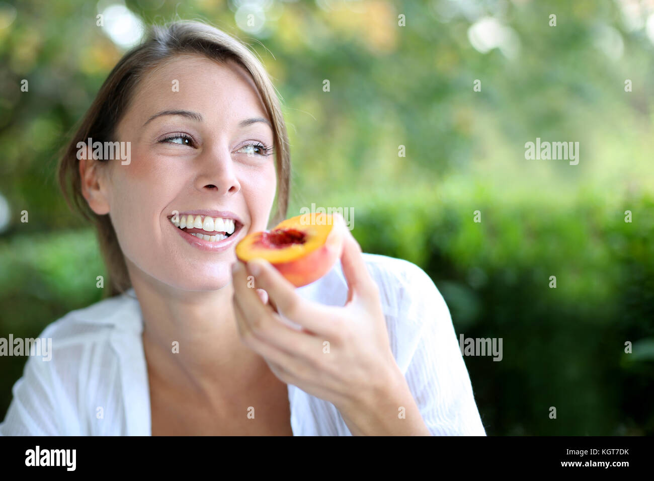 Smiling woman eating peach for breakfast Stock Photo - Alamy