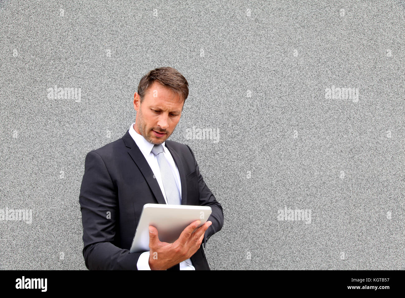 Businessman using electronic tablet leant against wall Stock Photo - Alamy
