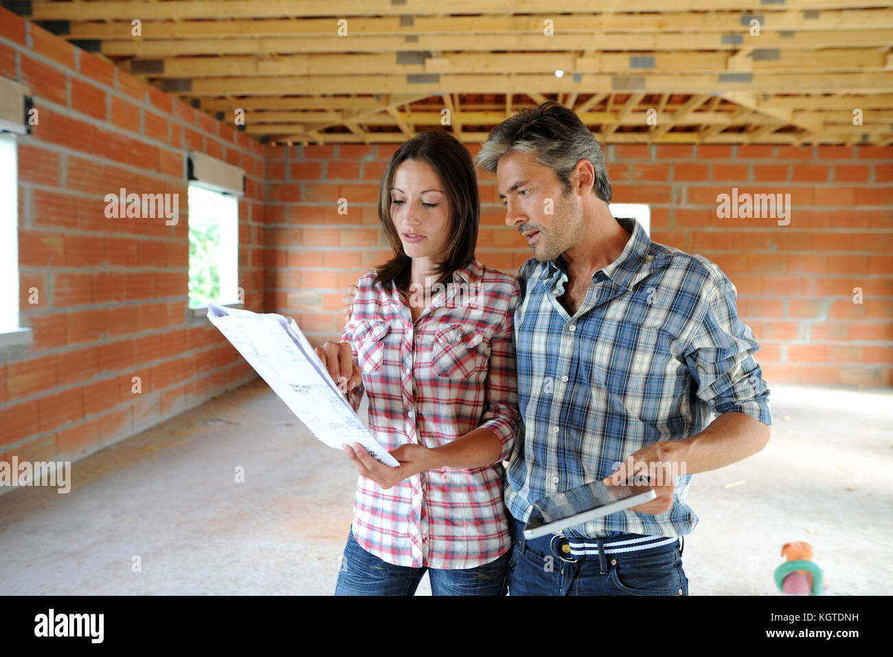 Cheerful couple standing inside house under construction Stock Photo ...