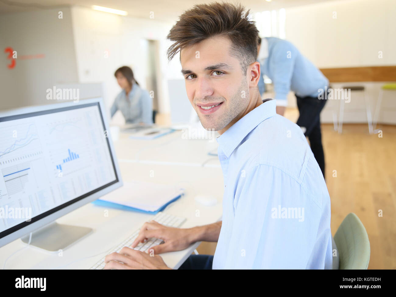 Office worker sitting in front of desktop, colleagues in background ...