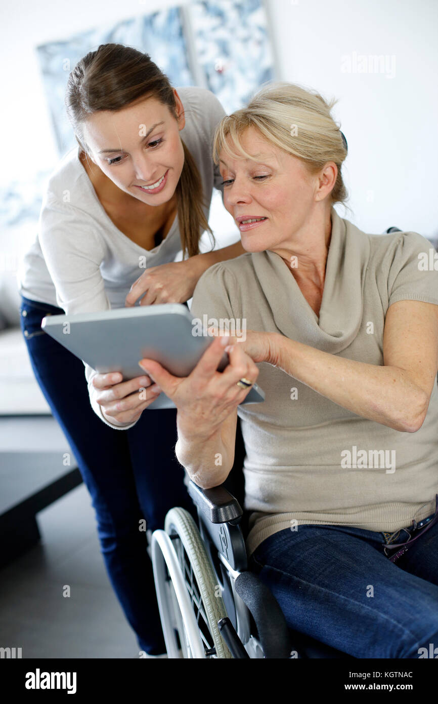 Girl showing tablet to elderly woman in wheelchair Stock Photo - Alamy
