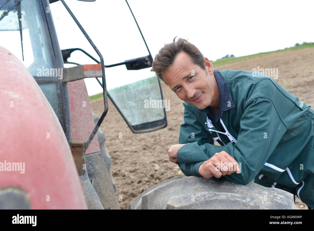 Smiling handsome farmer leaning on tractor Stock Photo - Alamy