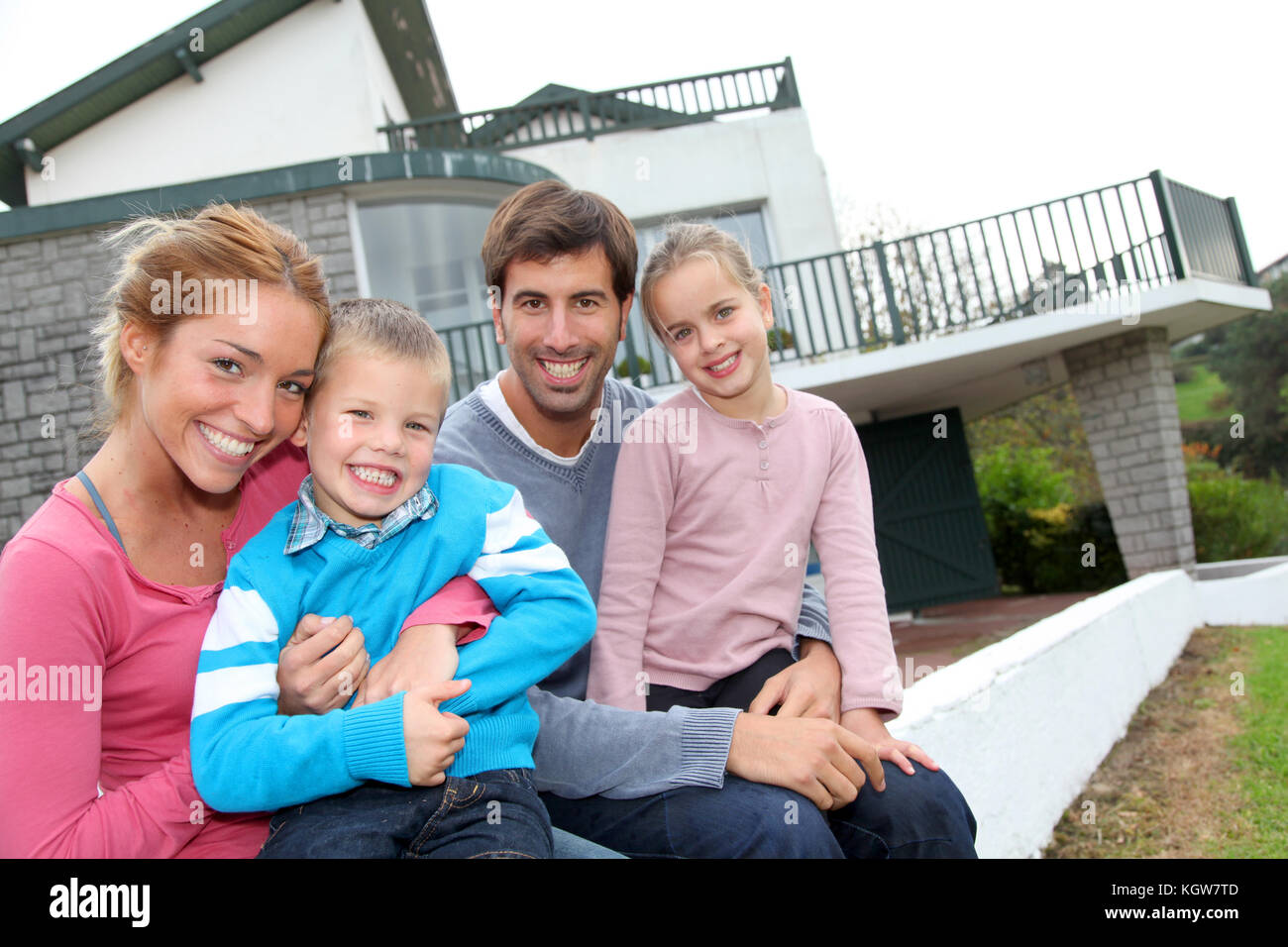 Happy family of 4 people sitting in front of new home Stock Photo - Alamy