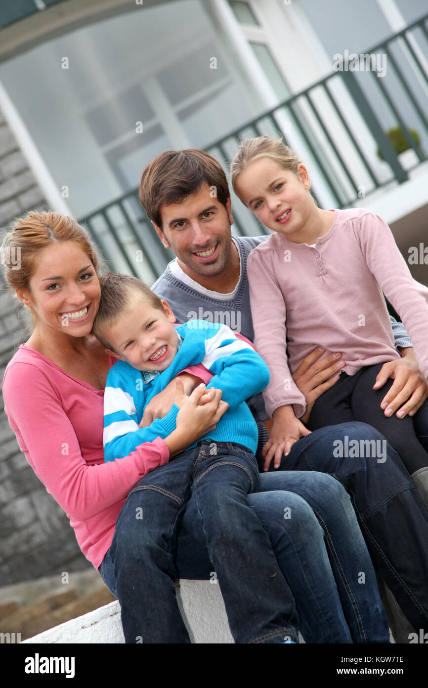 Happy family of 4 people sitting in front of new home Stock Photo - Alamy