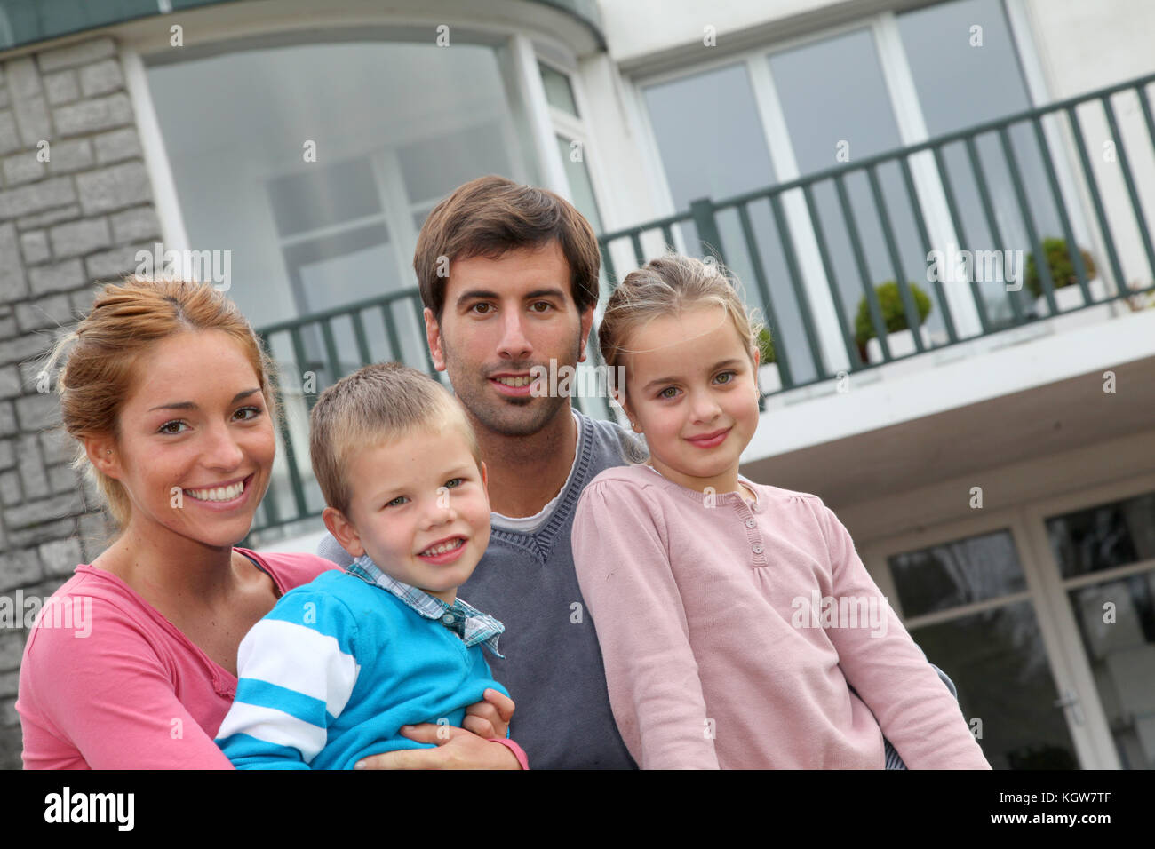 Happy family of 4 people sitting in front of new home Stock Photo - Alamy